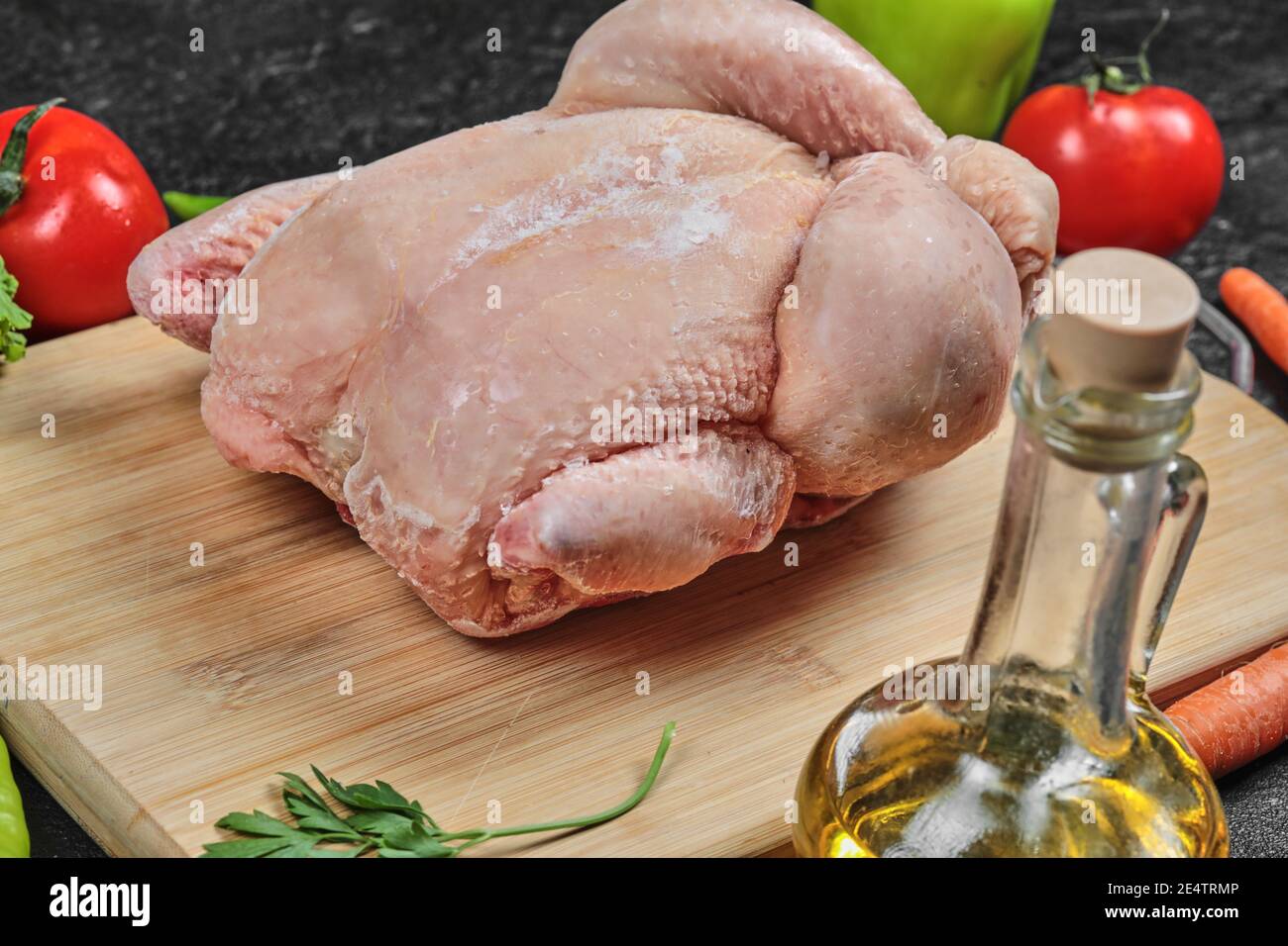 Raw whole chicken on wooden board with oil and tomatoes Stock Photo - Alamy