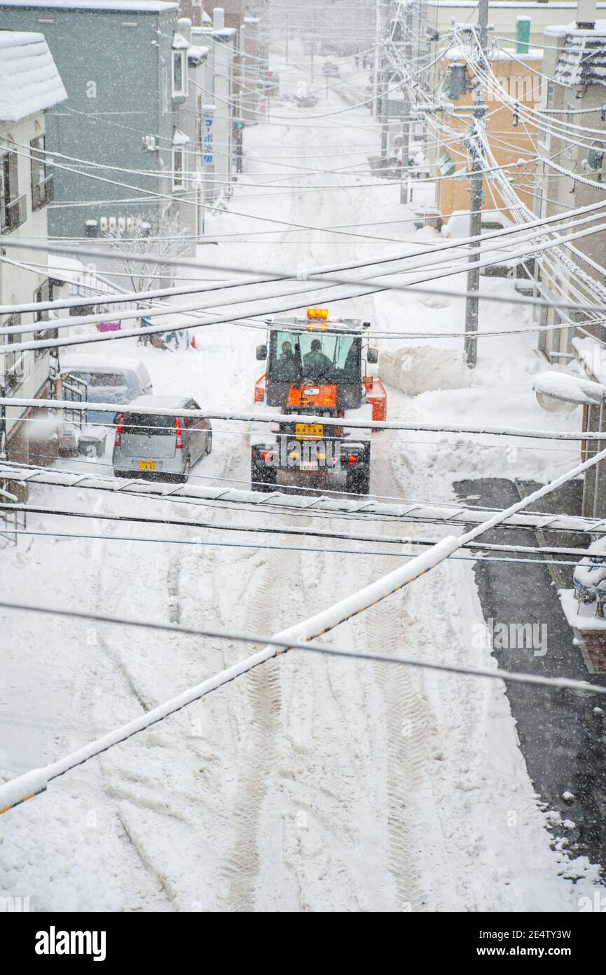 Snowplow tractor removing snow in a narrow Japanese street during a ...