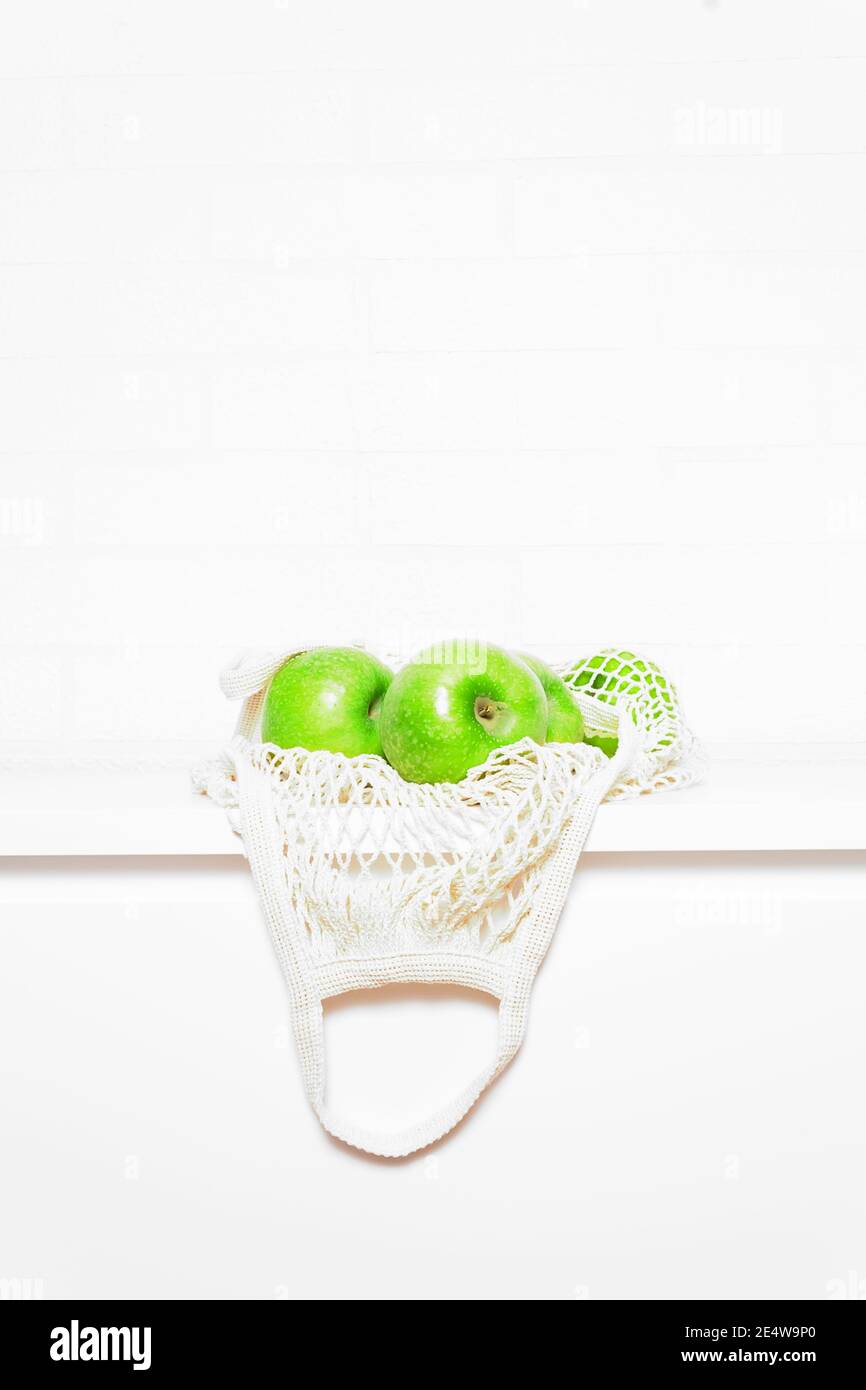 Green apples in eco mesh bag on white kitchen table. Market shopping ...