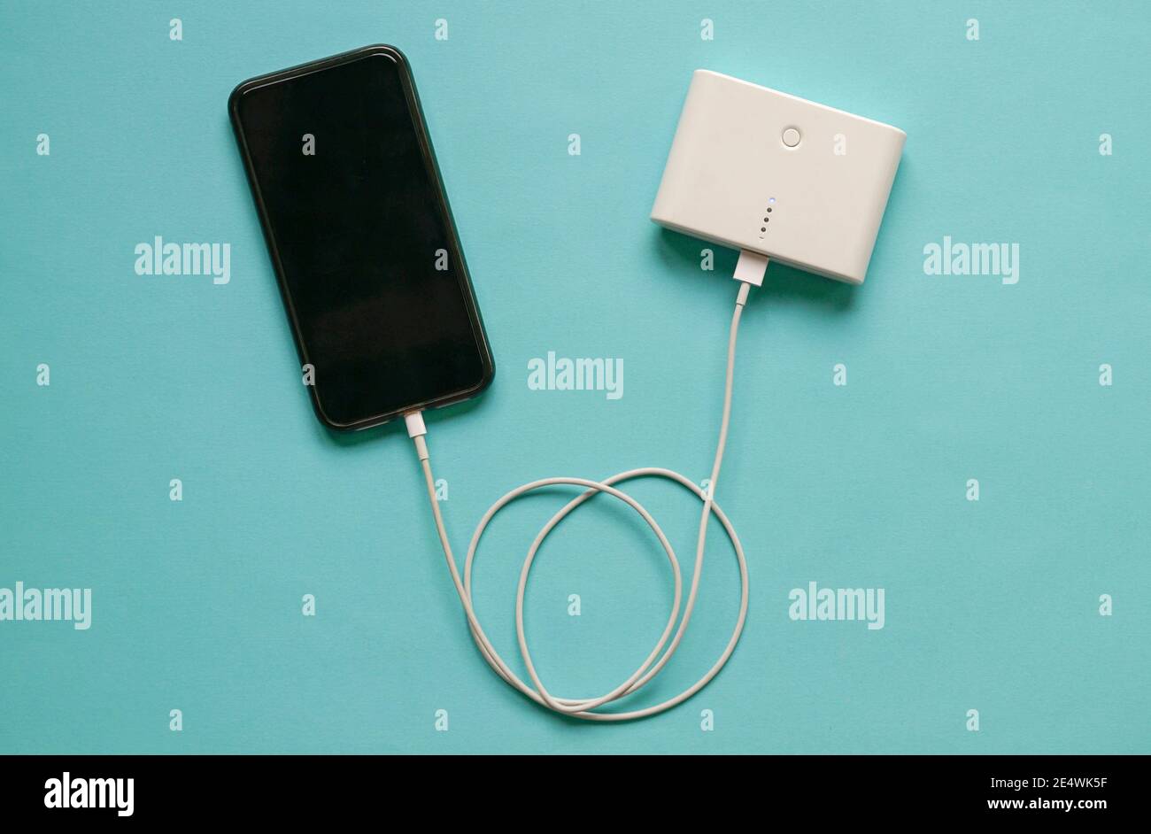 Cellphone getting charged from power bank. Isolated. On blue background ...