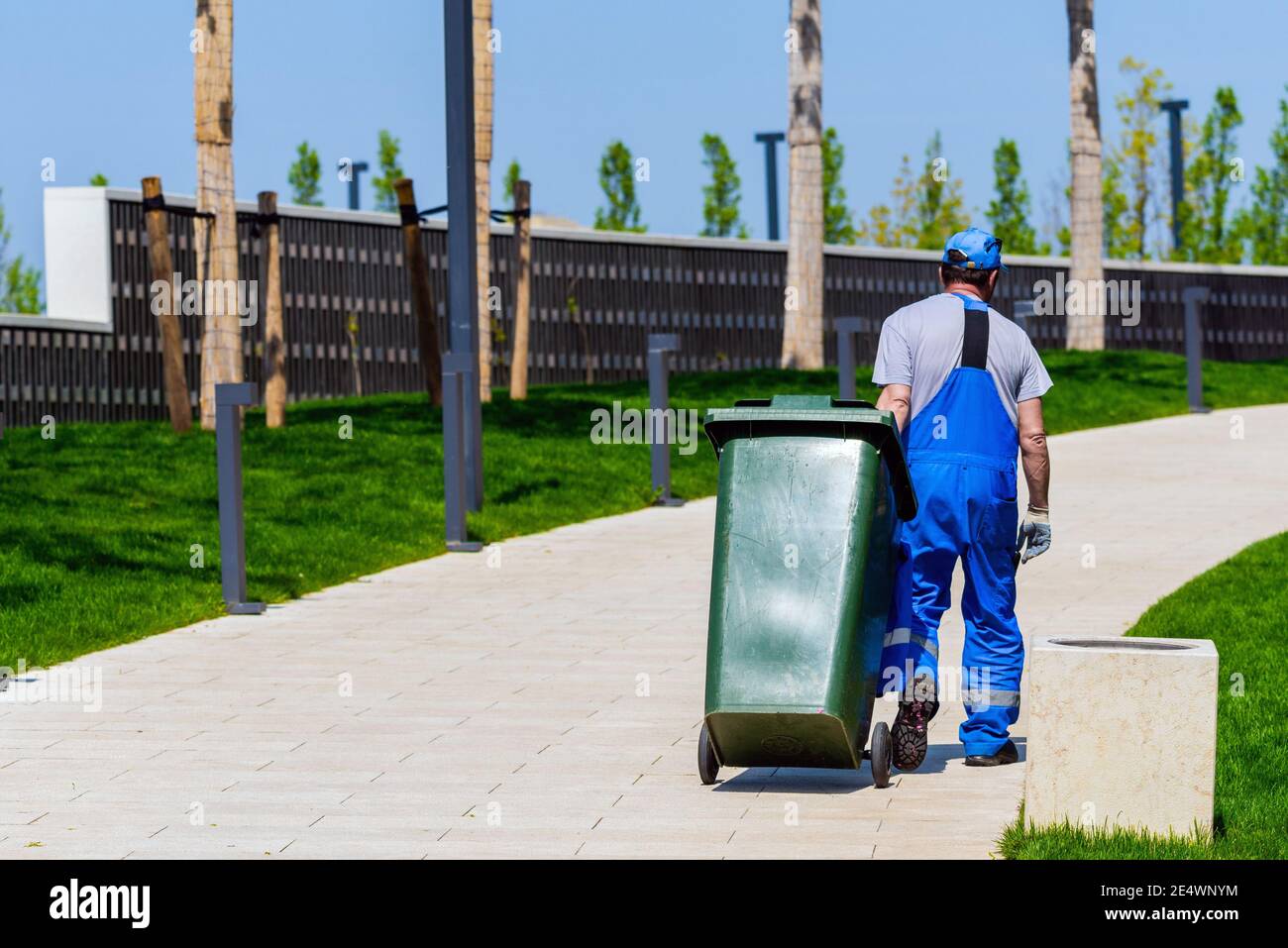 Janitor rolls trash can on wheels. Cleaning service in modern park ...