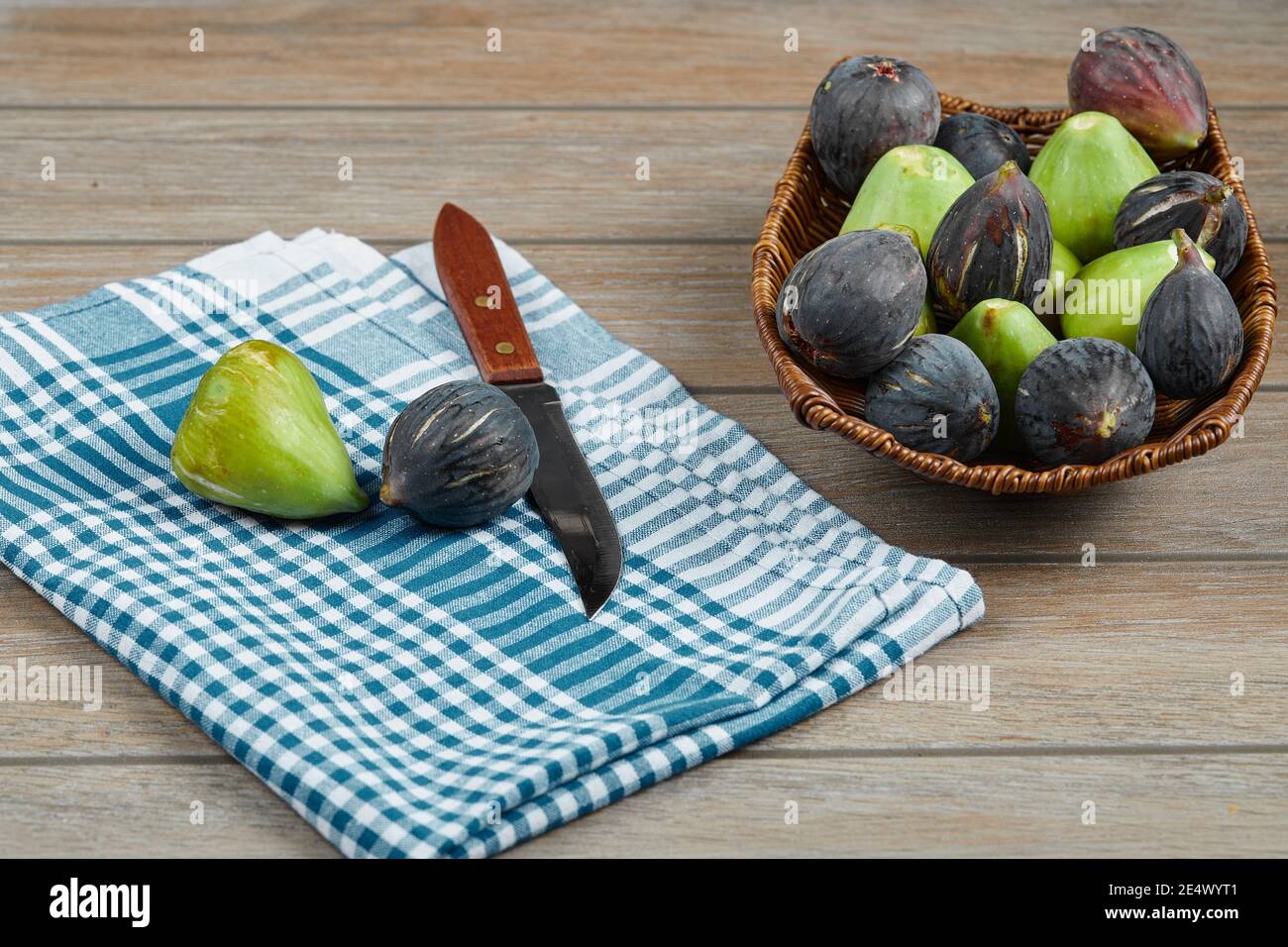 A bowl of mixed figs on a wooden table with a knife and a tablecloth ...