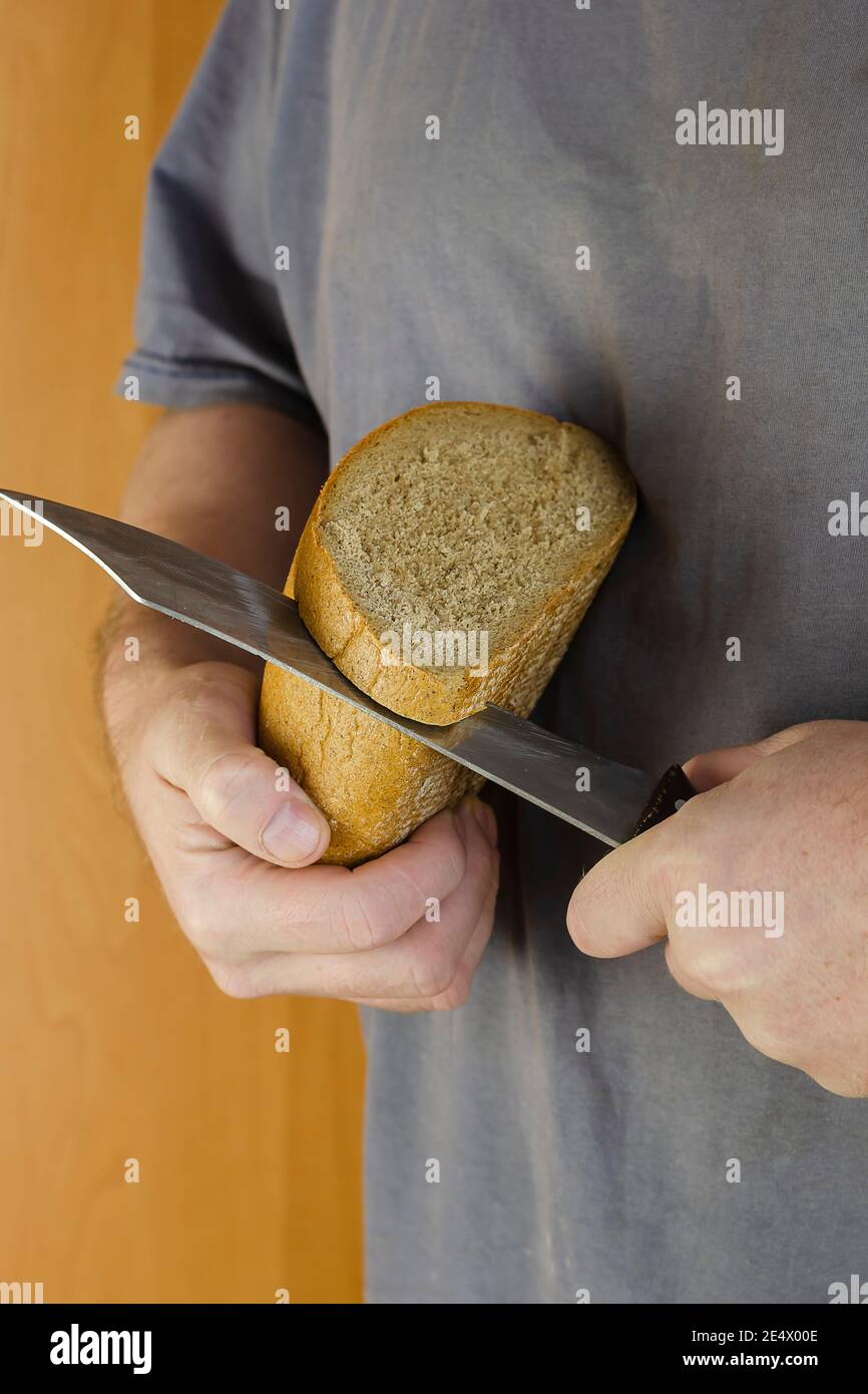 A man cradles half a loaf of bread and a knife. Slices rye bread with a ...