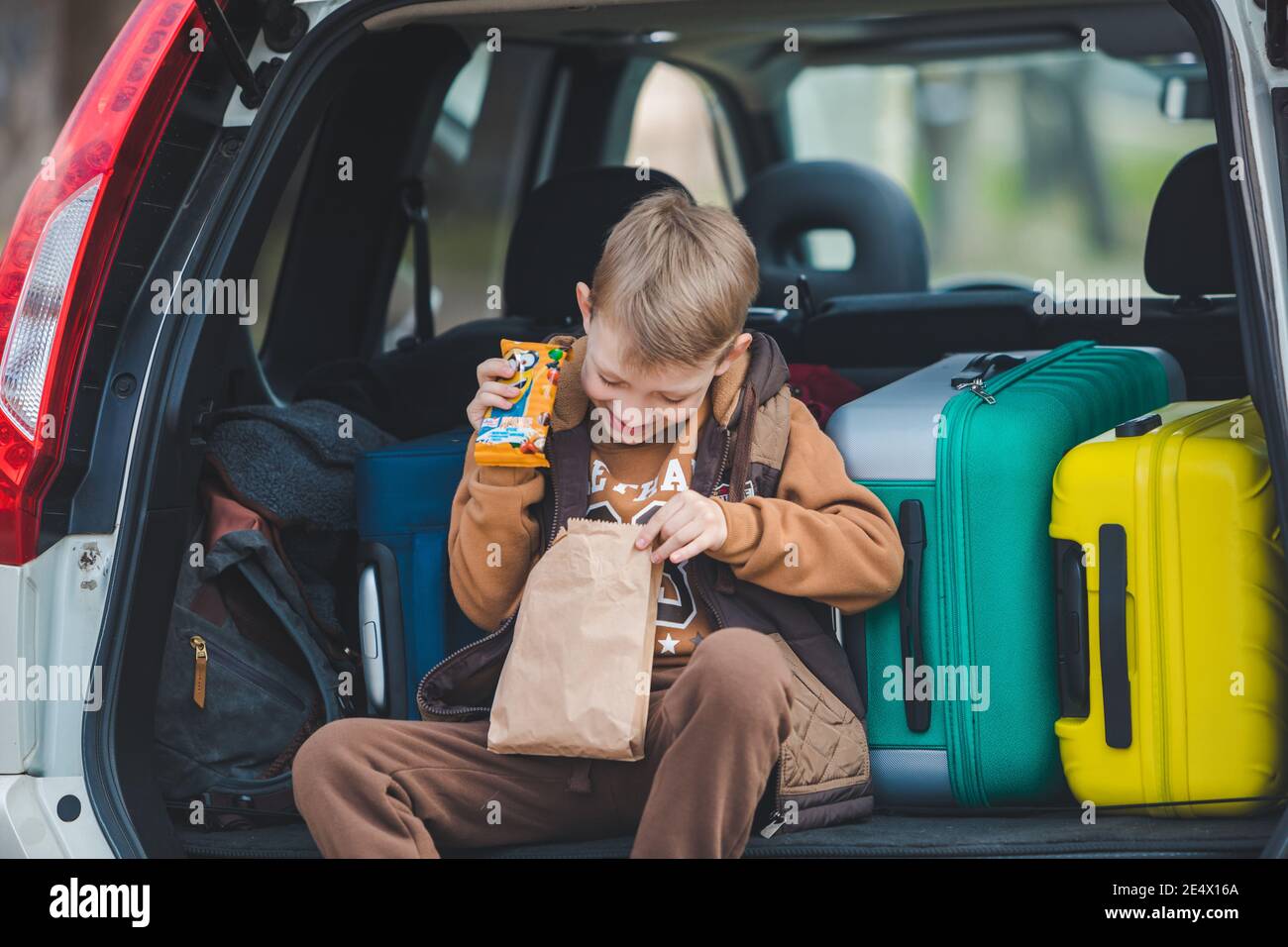 little kid looking into paper bag with candies sitting in car trunk ...