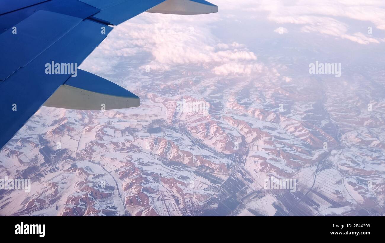 Air plane flies among the clouds over snowy capped mountains. Winter ...