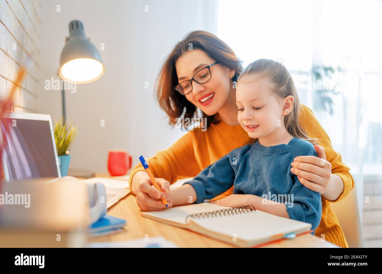 Happy child and adult are sitting at desk. Girl doing homework or ...