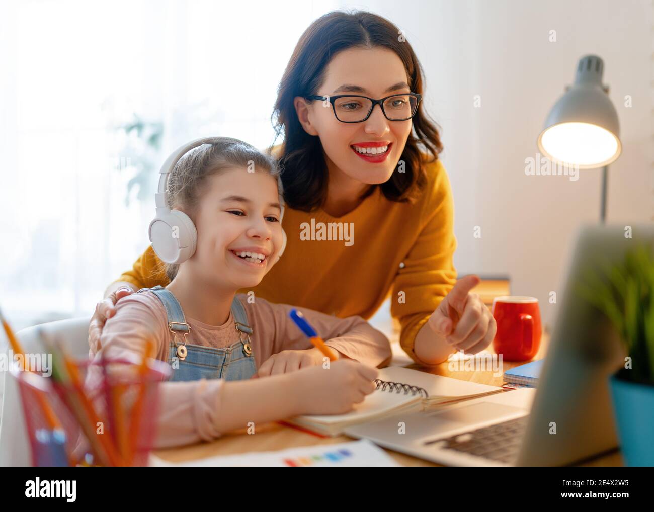 Back to school. Happy child and adult are sitting at desk. Girl doing ...