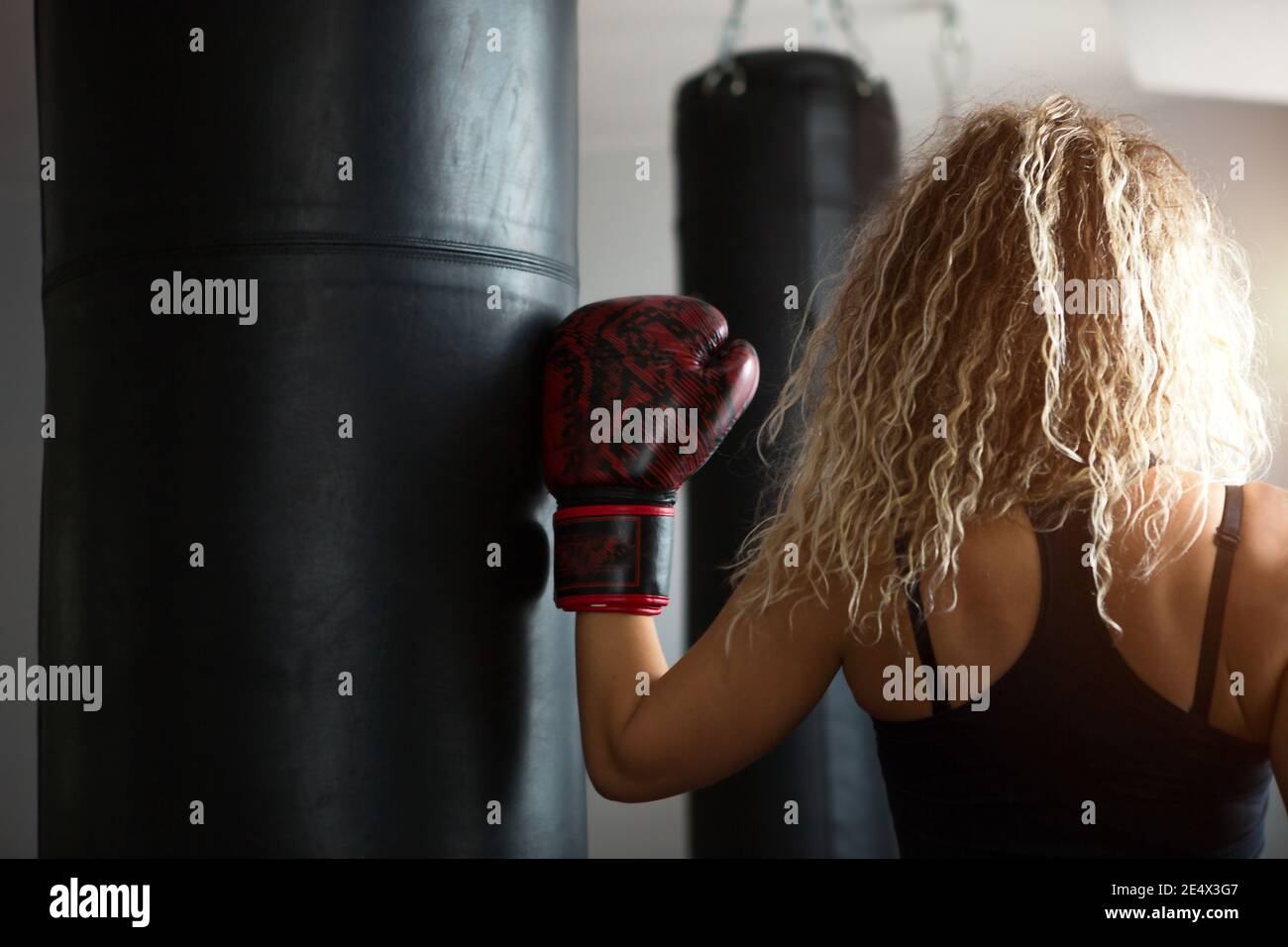 A woman with long curly blonde hair with a boxing glove near a punching ...