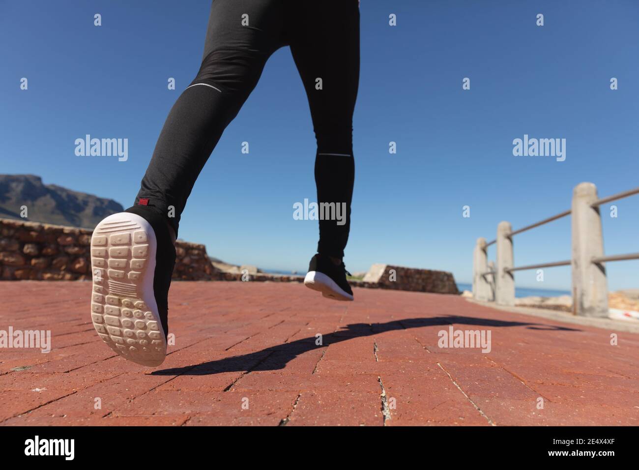 Low section of senior man exercising running on coastal path on sunny ...