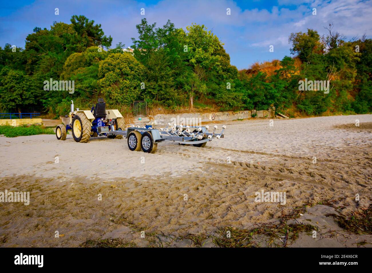 Tractor with empty trailer is parked on the sandy beach, waiting for ...