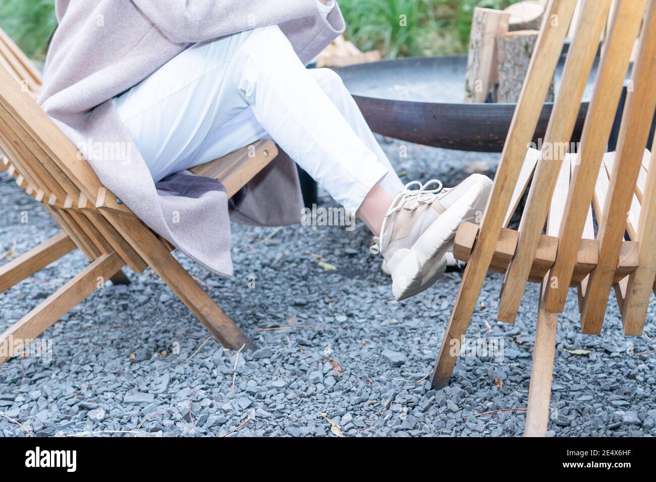 A woman in a coat and sneakers sitting on a chair leaned her leg on ...