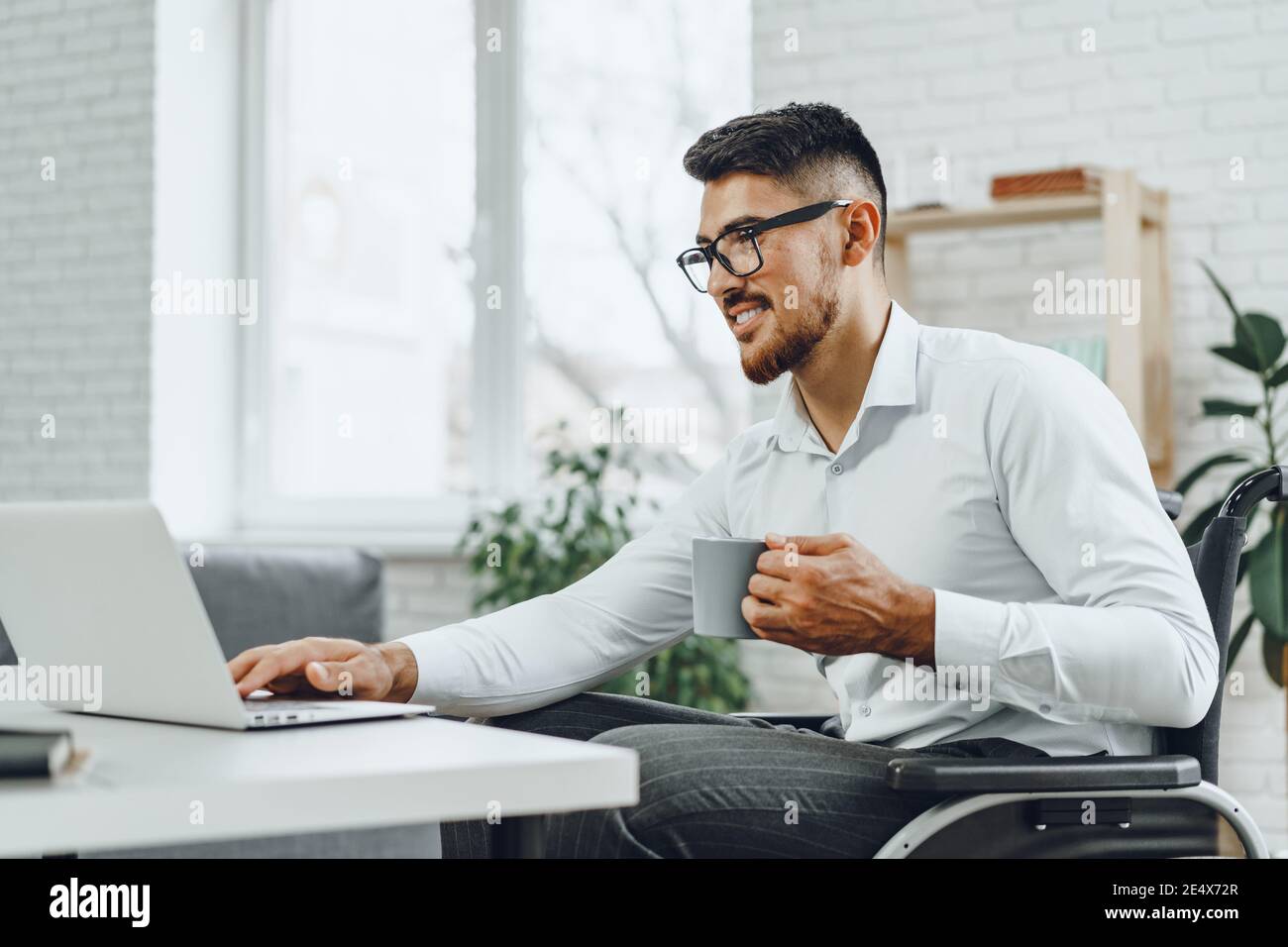 Positive disabled young man in wheelchair working in office Stock Photo ...