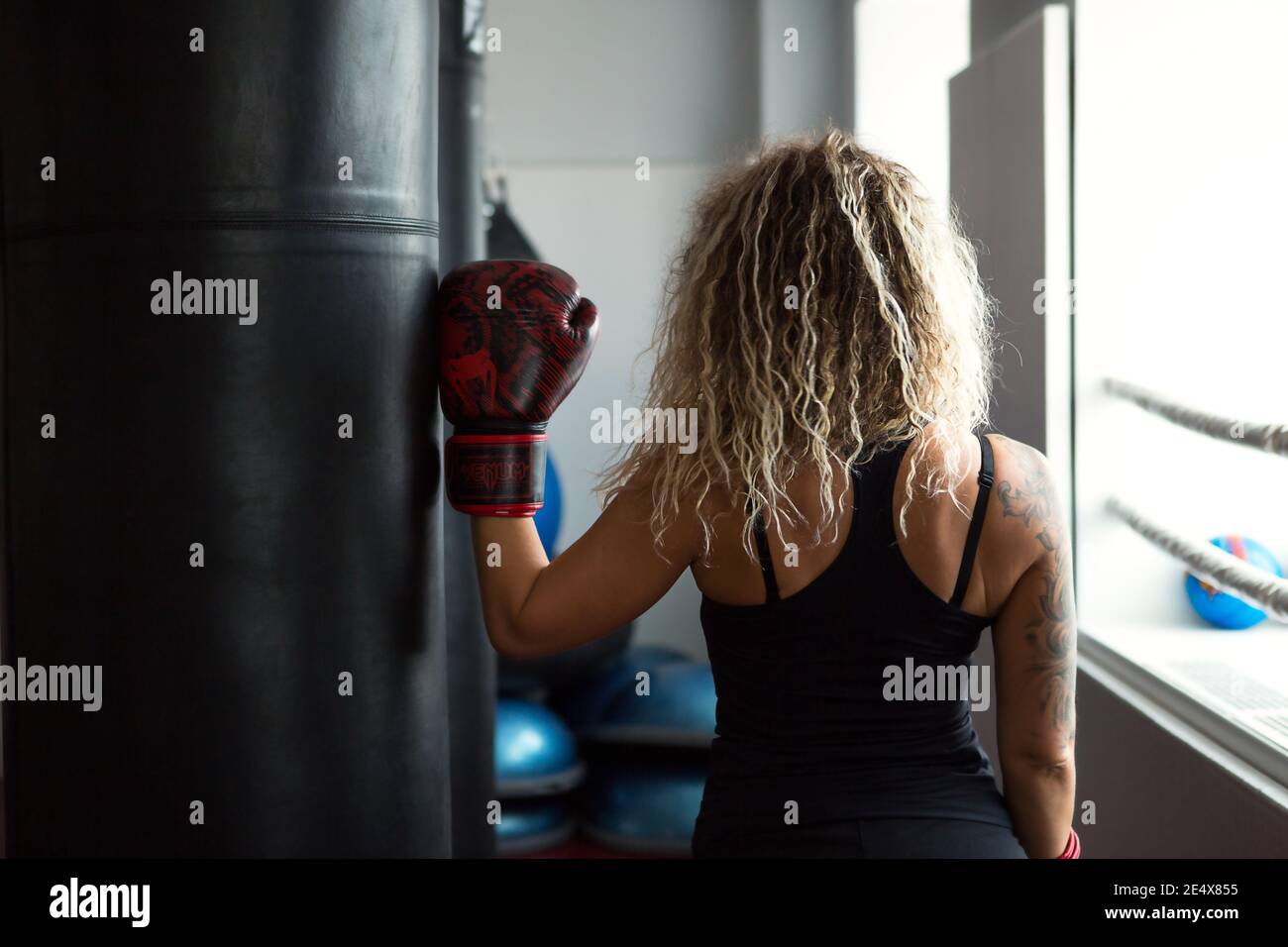 A woman with long curly blonde hair with a boxing glove near a punching ...