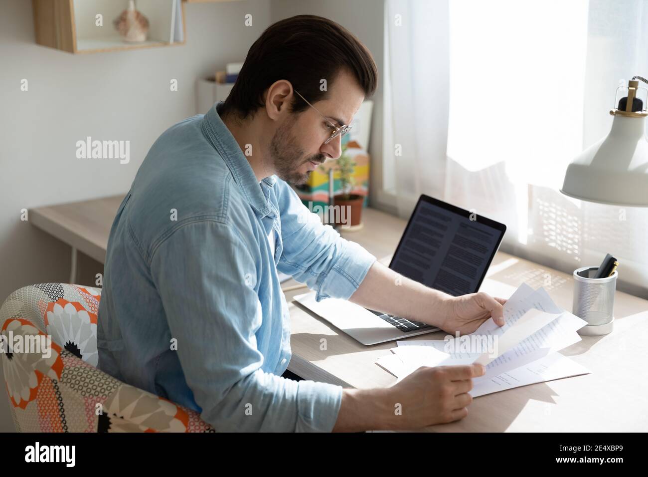 Concentrated young man remote employee doing paperwork by laptop screen ...