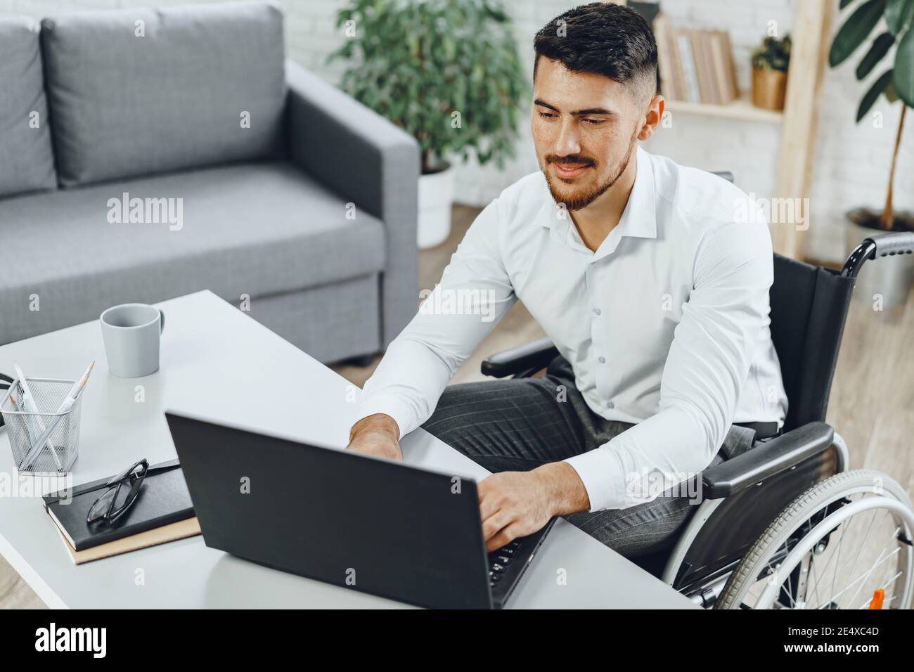 Positive disabled young man in wheelchair working in office Stock Photo ...