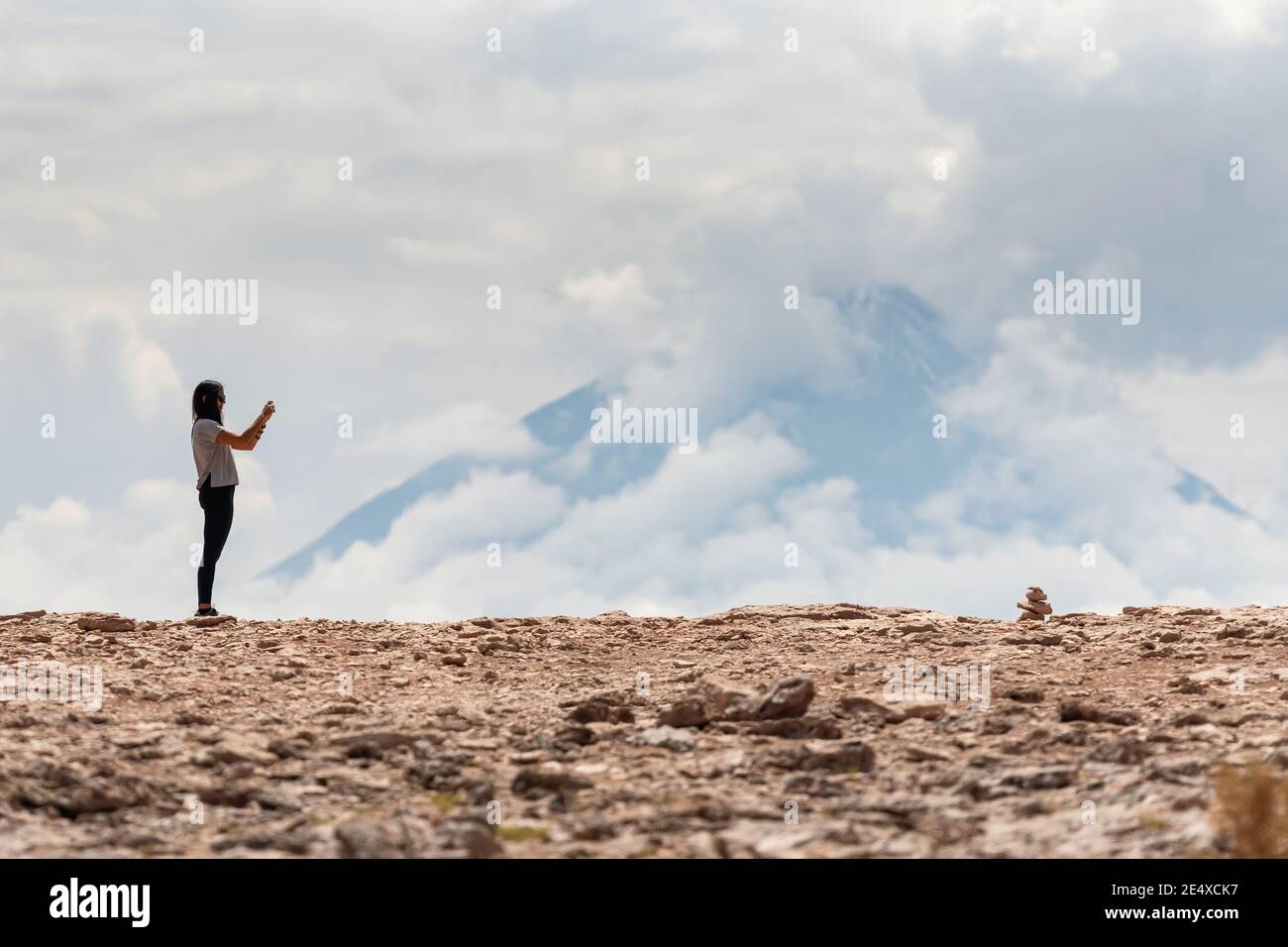Woman taking pictures of stack of stone against cloudy sky and ...