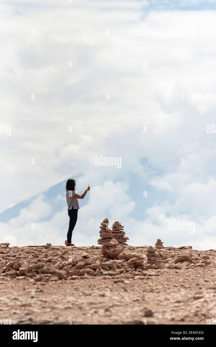 Woman taking pictures of stack of stone against cloudy sky and ...