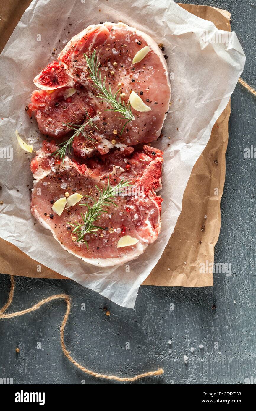 Two raw pork steaks grey stone background with rosemary and spices. Top ...