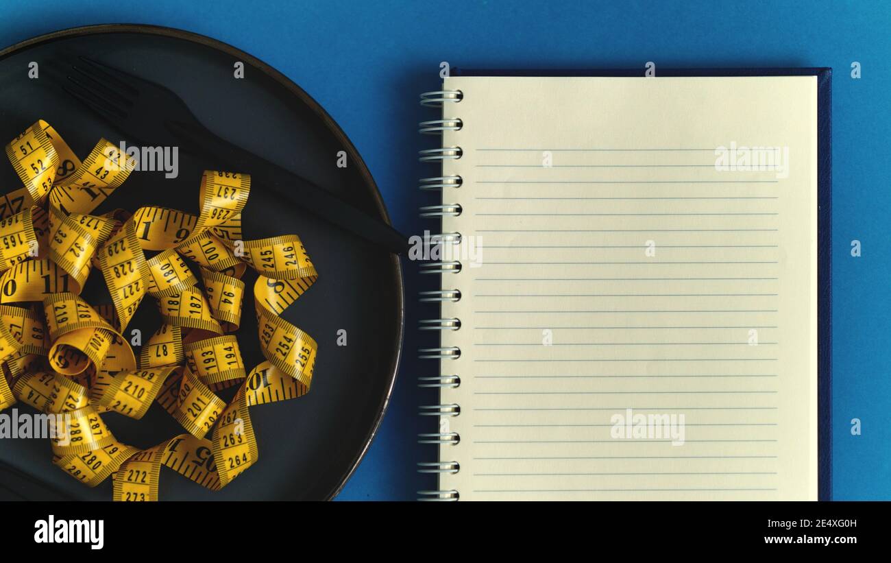 Top view of blank paper notebook next to tape measurement on a plate ...
