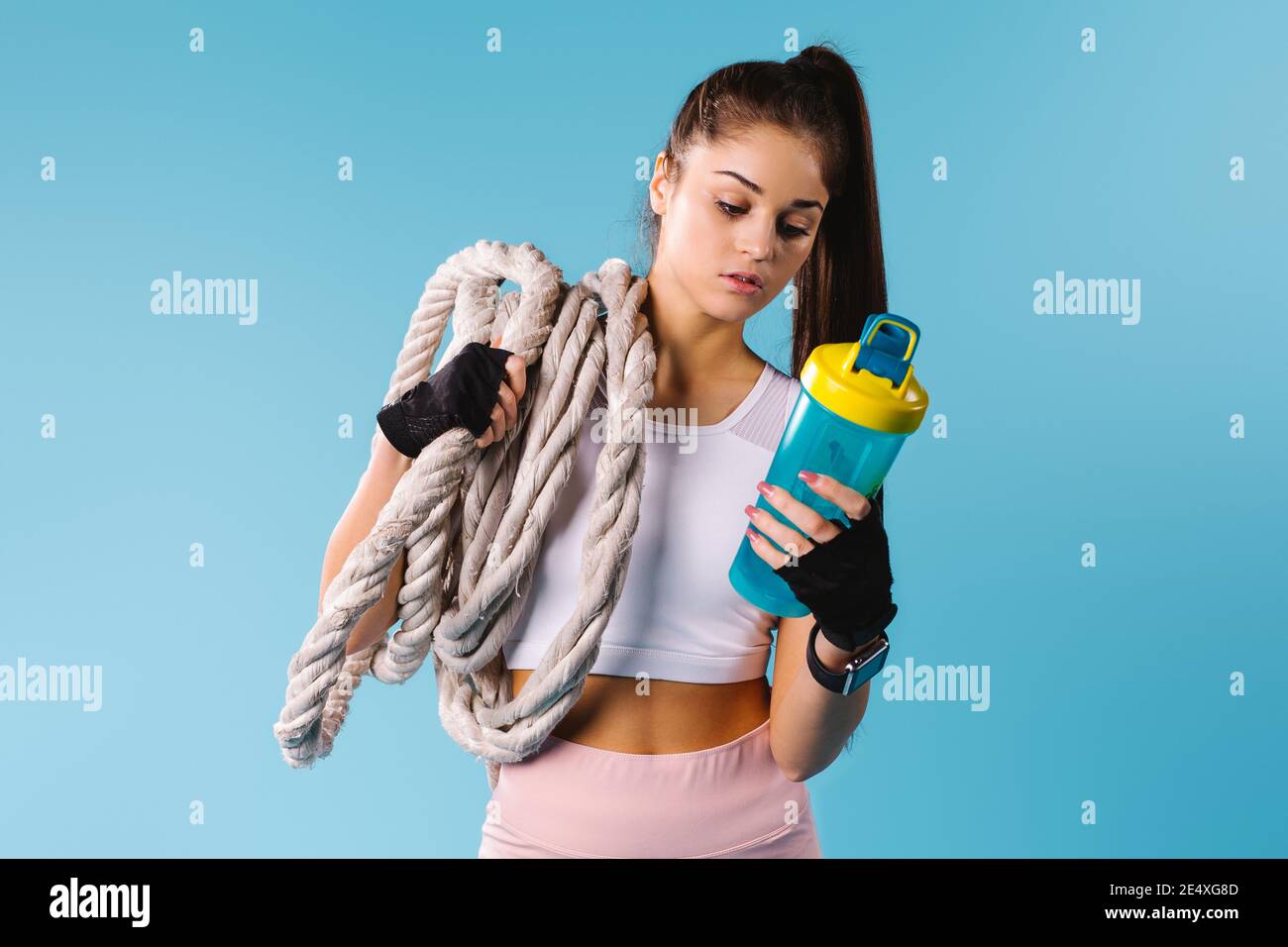 Sporty girl with a rope on her shoulder and with a protein shake in her ...