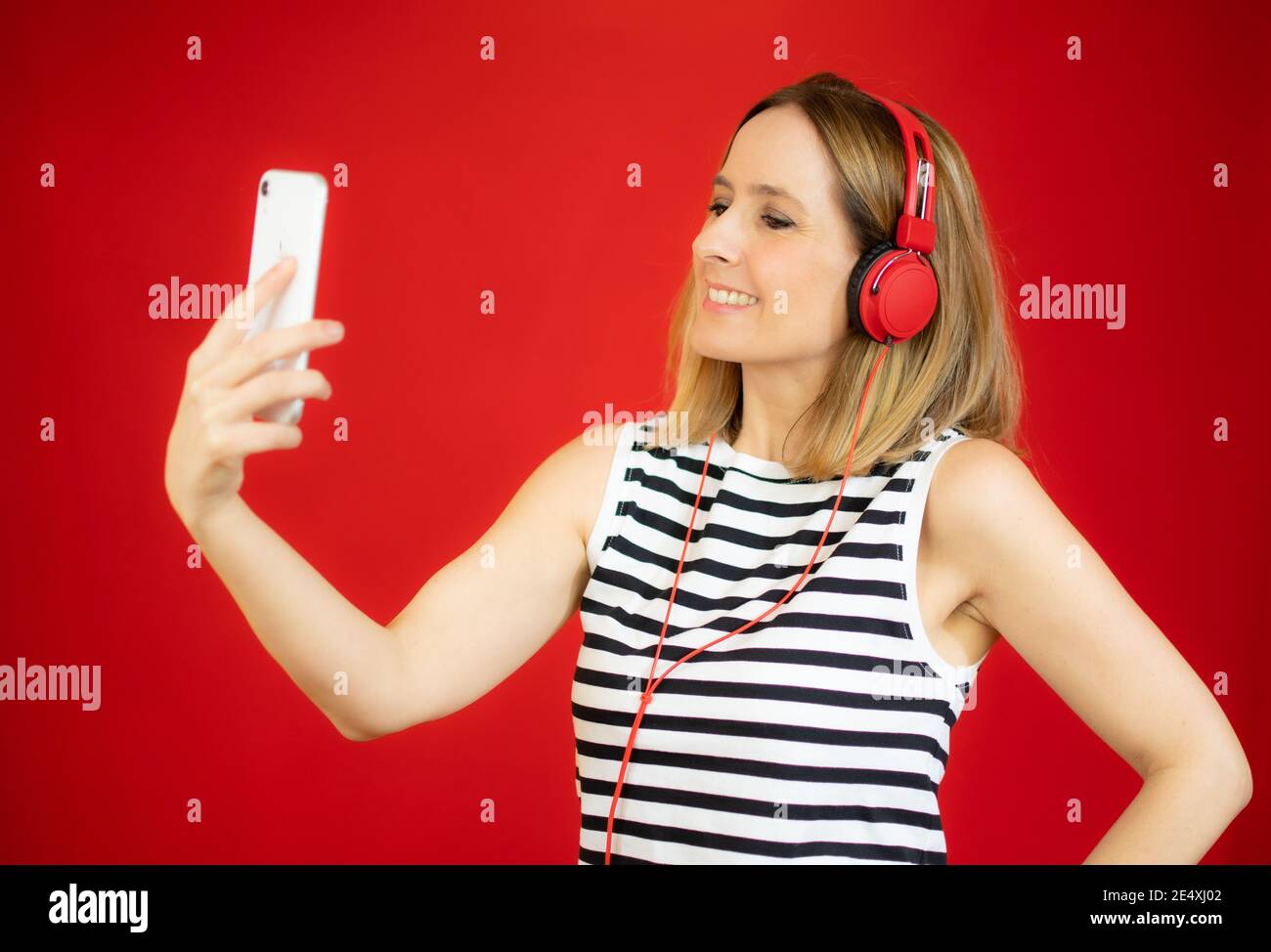 Woman holding cellphone listening to music In Earphones over red ...