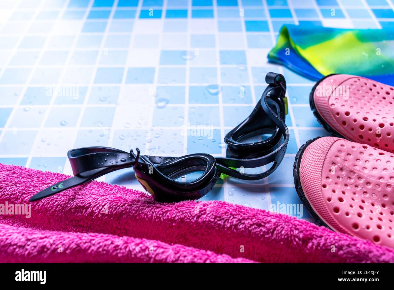 Closeup of pool shoes, goggles, cap, and a towel on blue-tiled surface ...