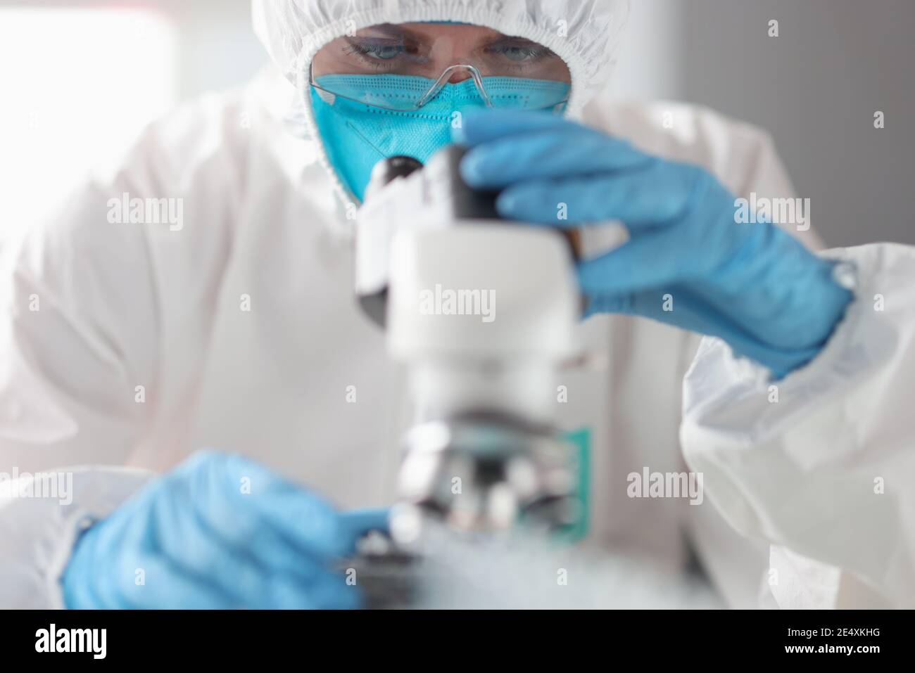 Doctor in protective suit and glasses looks through microscope Stock ...