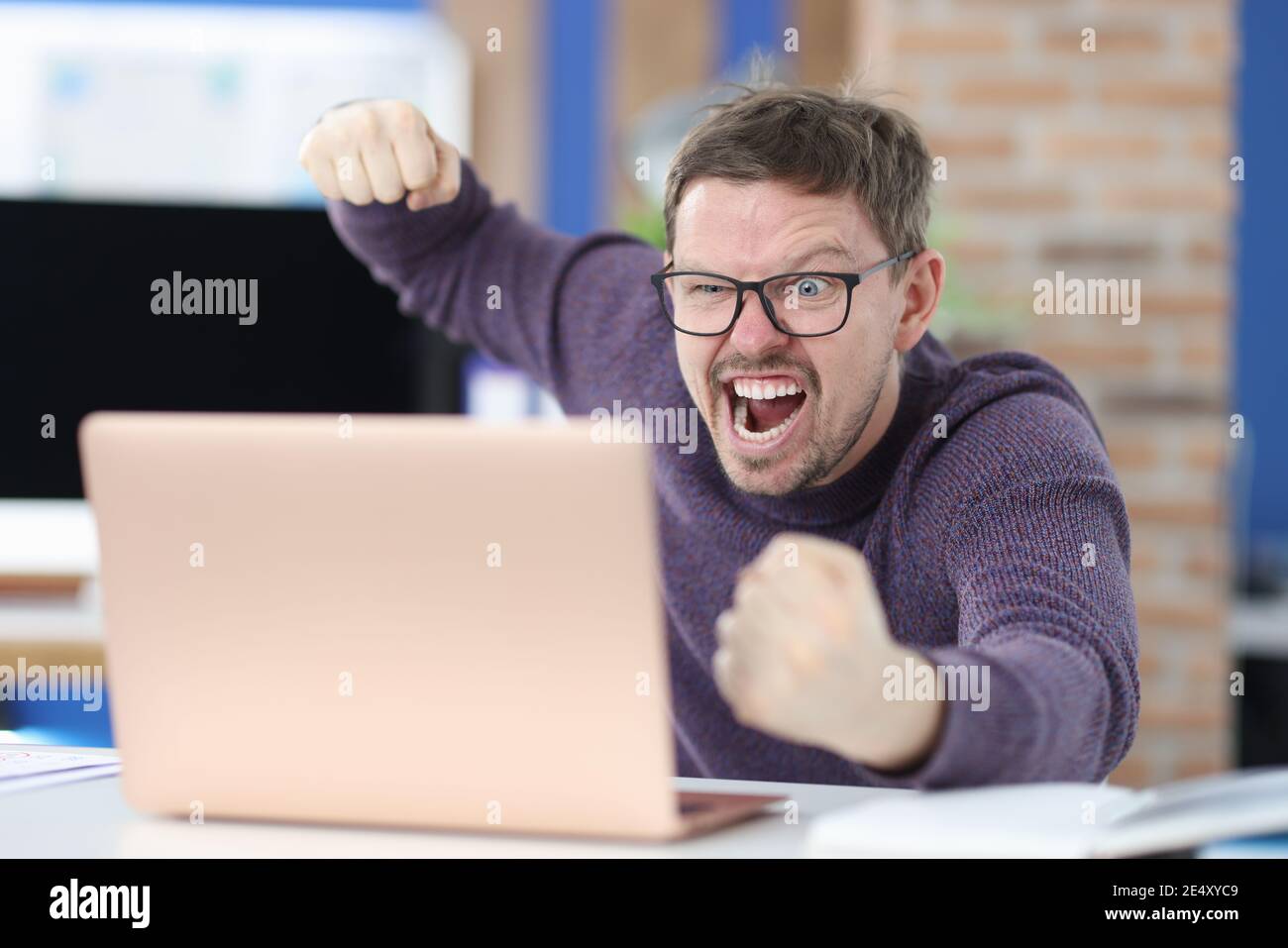 Angry man with glasses waves his fist at laptop monitor Stock Photo - Alamy