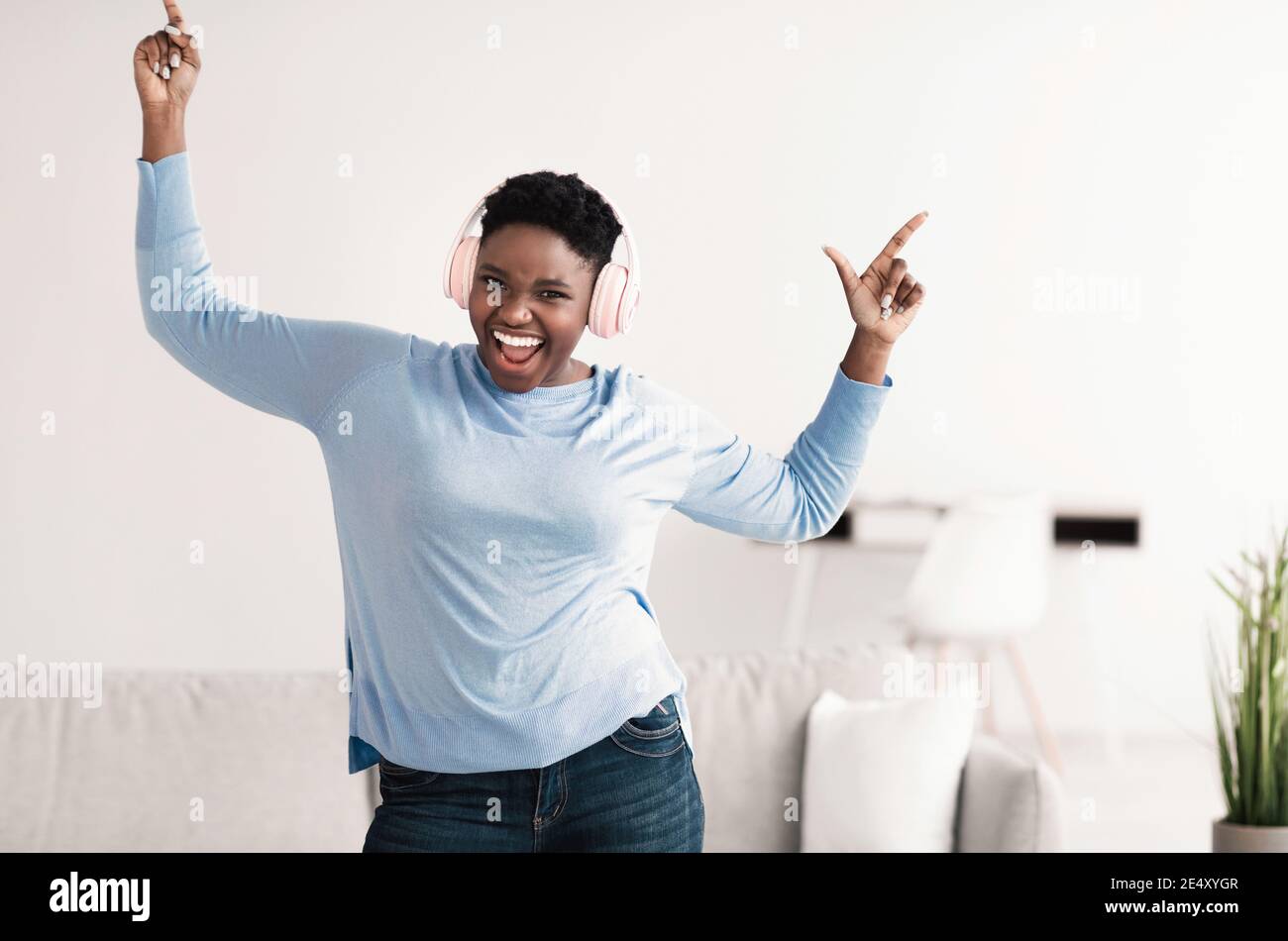 Joyful black woman listening to music in headphones and dancing Stock ...