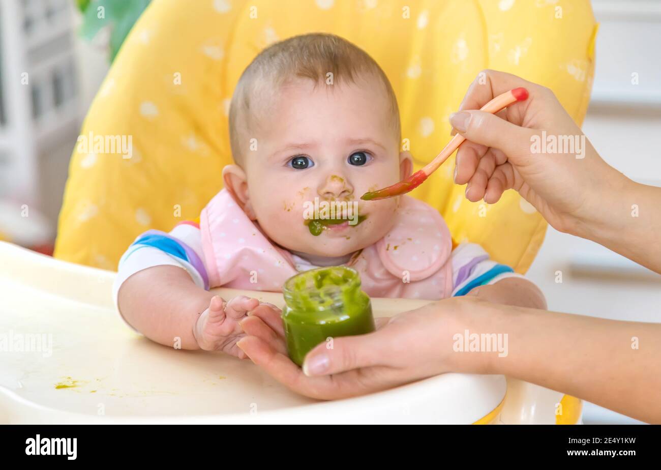 Little baby is eating broccoli vegetable puree. Selective focus. People ...