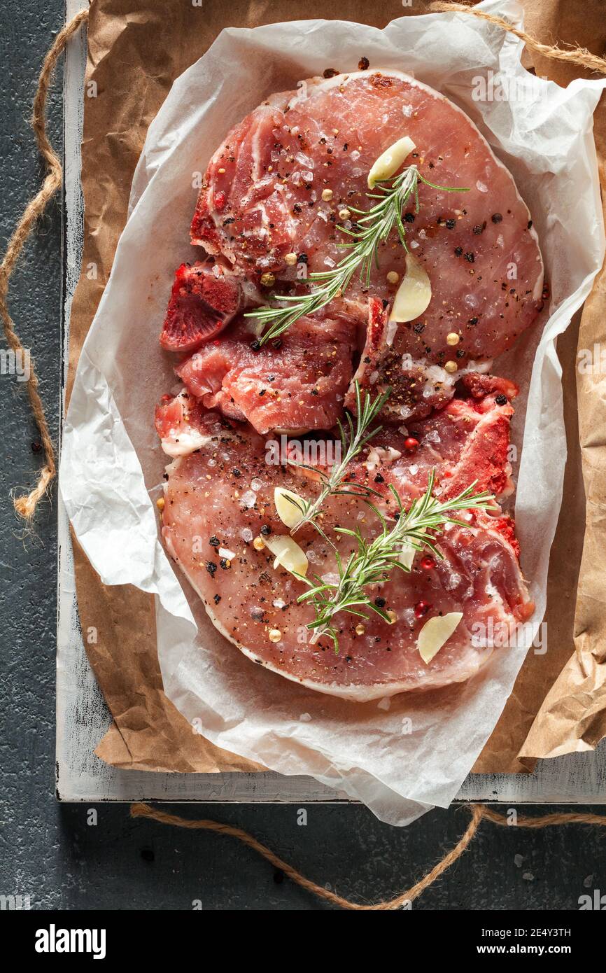 Two raw pork steaks grey stone background with rosemary and spices. Top ...