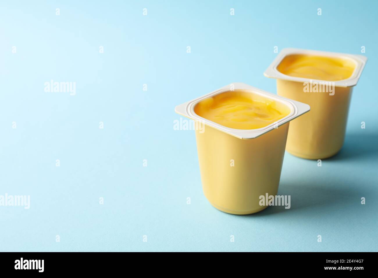 Plastic cups of yellow yogurt on blue background Stock Photo - Alamy