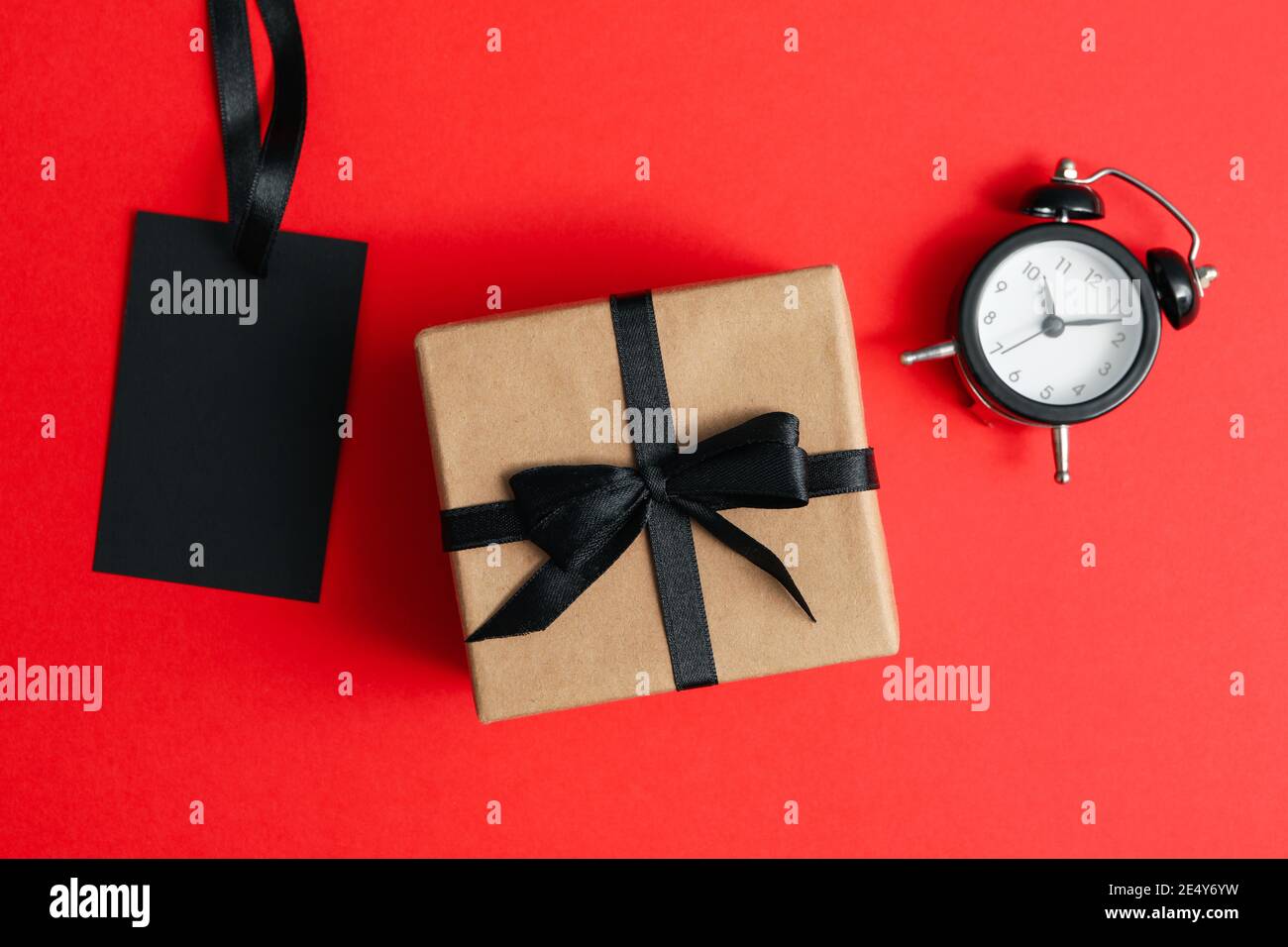 Alarm clock, gift box and tag on red background Stock Photo - Alamy