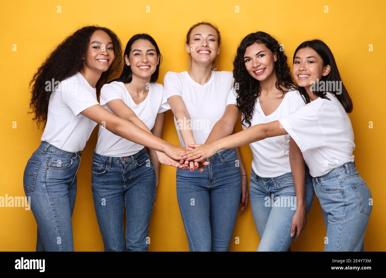 Five Cheerful Diverse Women Holding Hands Standing On Yellow Background ...