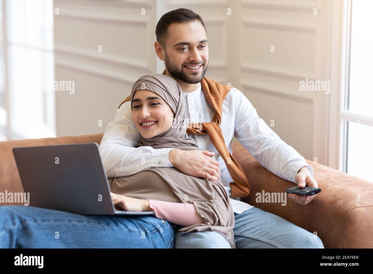Muslim Couple Relaxing Using Laptop And Watching TV At Home Stock Photo ...