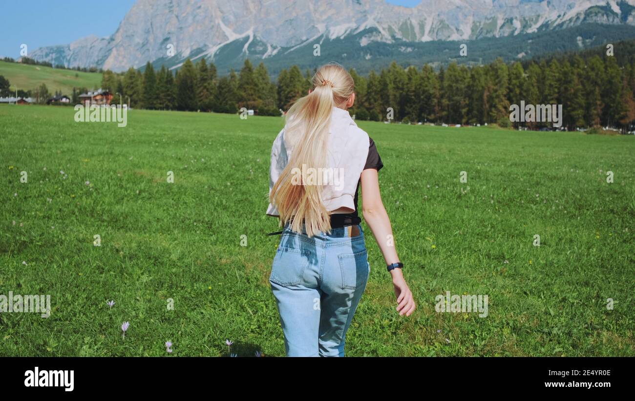 Back view of woman running on the field with mountains in front ...