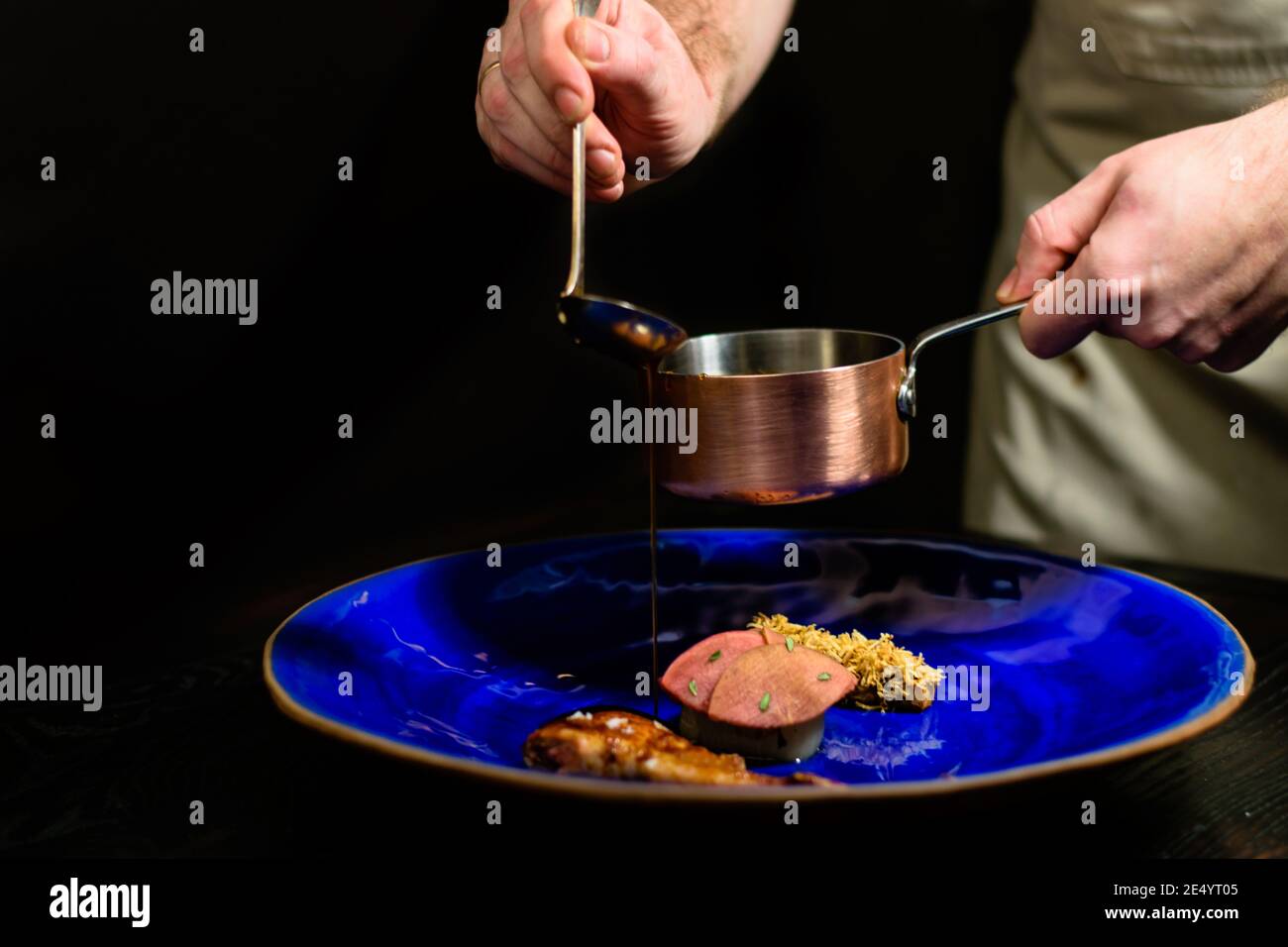 Chef pouring over a souce of a dish of quail, onion, apple, celery root ...