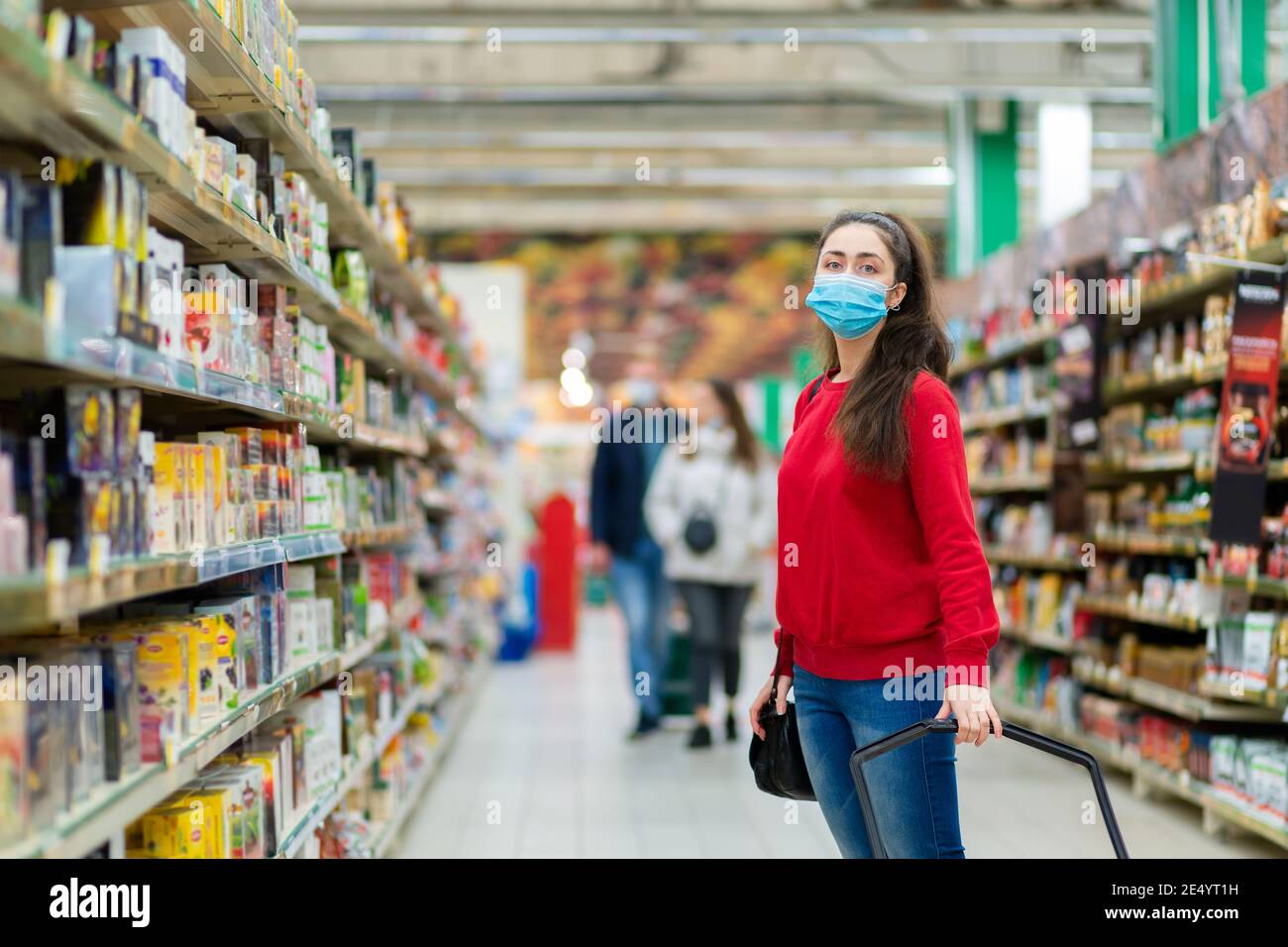 A young woman in a medical mask poses in the aisle of a supermarket ...