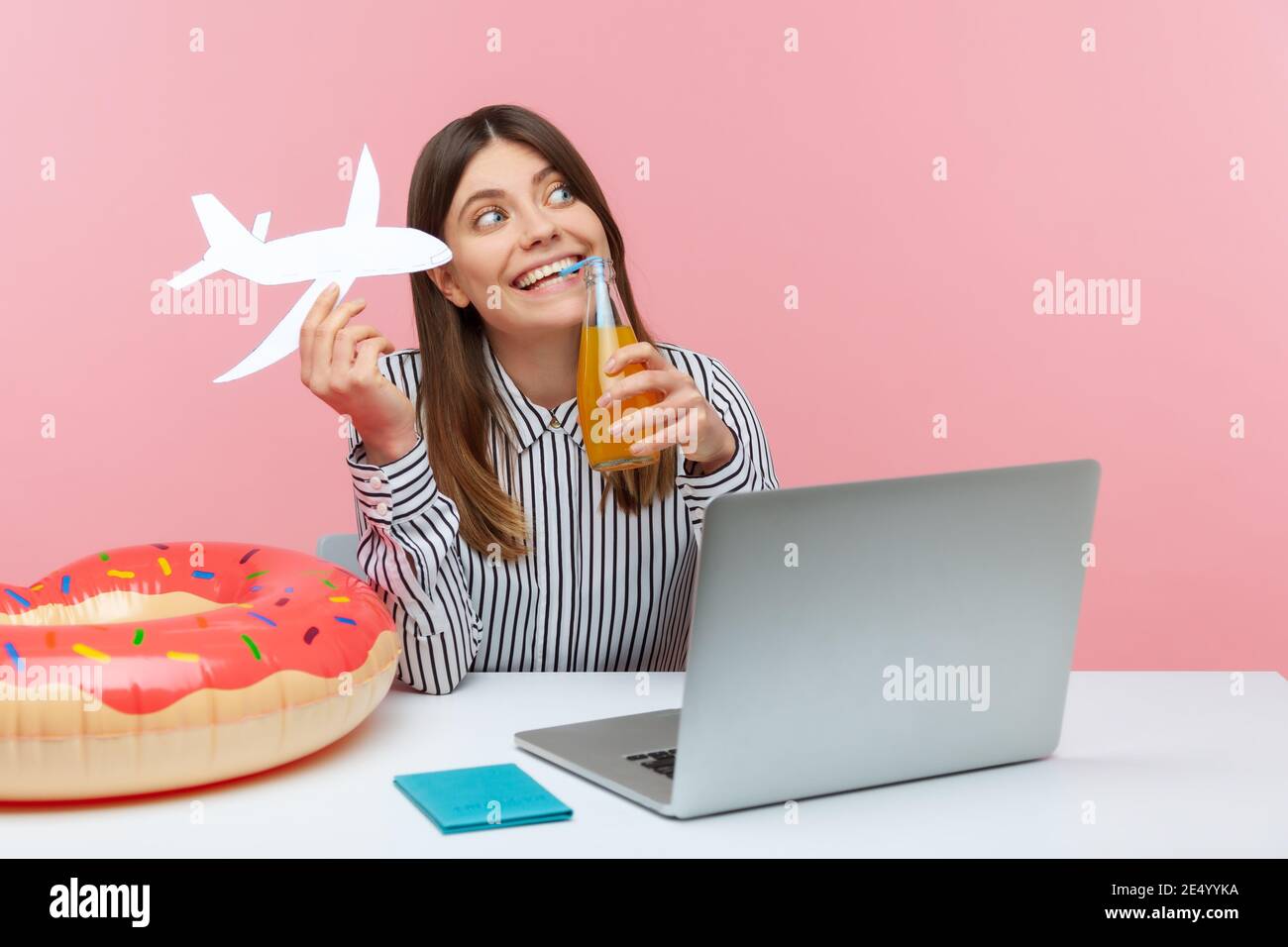 Positive woman drinking lemonade holding paper plane in hand planning ...