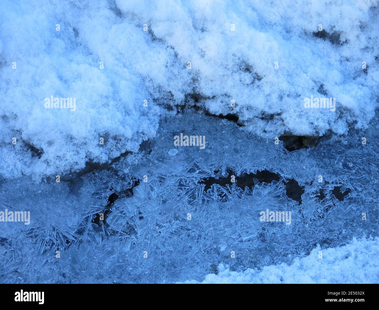 Abstract photo of white snow alongside a stream of frozen water full of ...