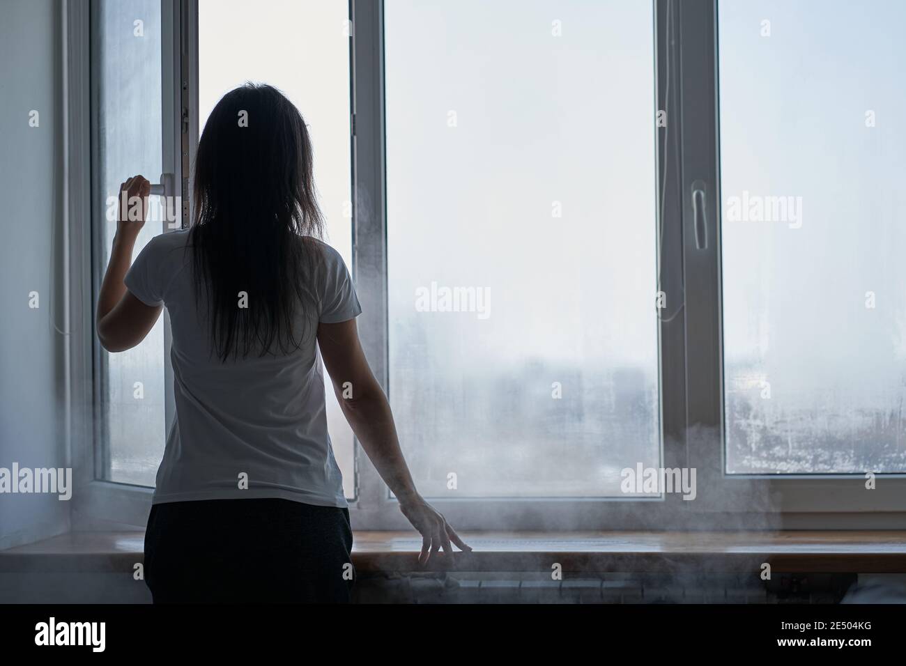 Cold winter weather. Woman step to window, open it and frosty air ...