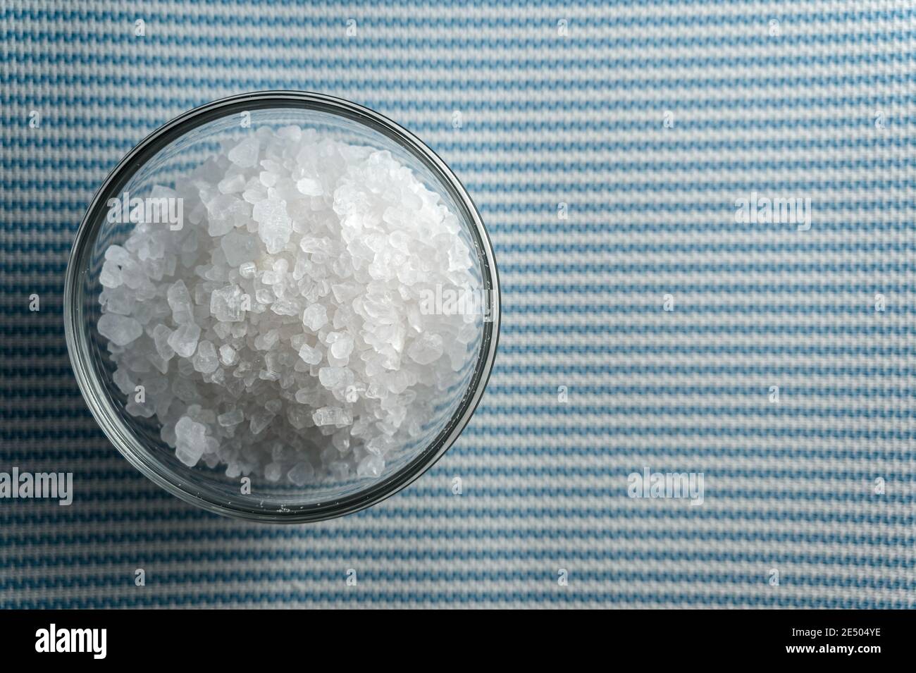 Glass bowl of sea salt on white and blue background with empty space ...