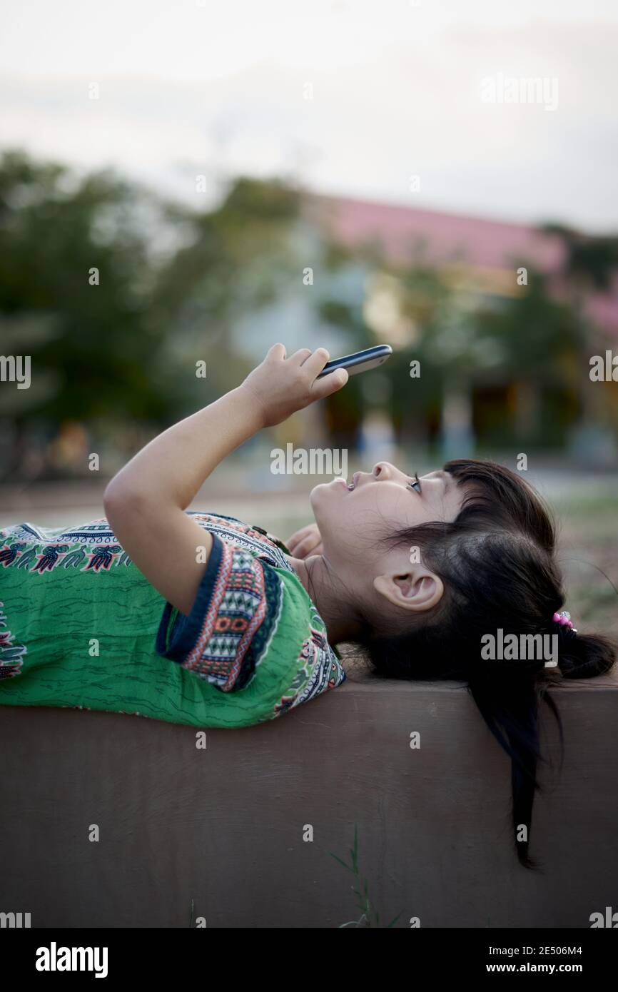 Cute little girl lying down and playing with mobile phone at public ...