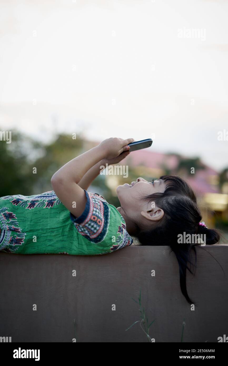 Cute little girl lying down and playing with mobile phone at public ...