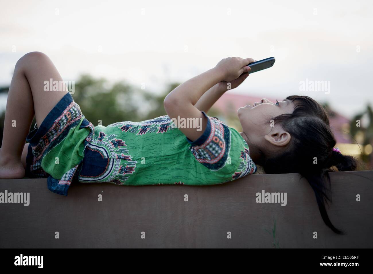 Cute little girl lying down and playing with mobile phone at public ...