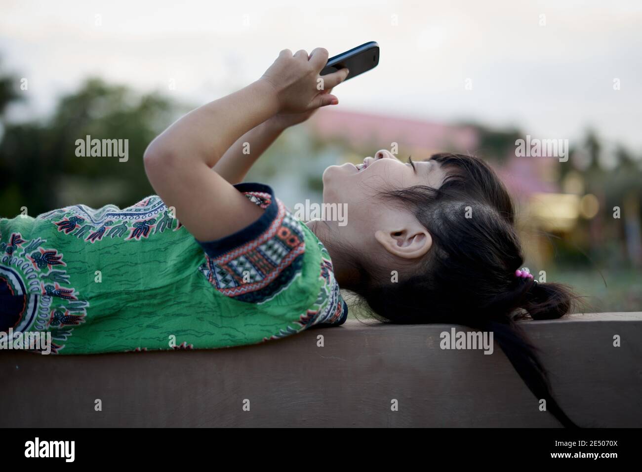 Cute little girl lying down and playing with mobile phone at public ...