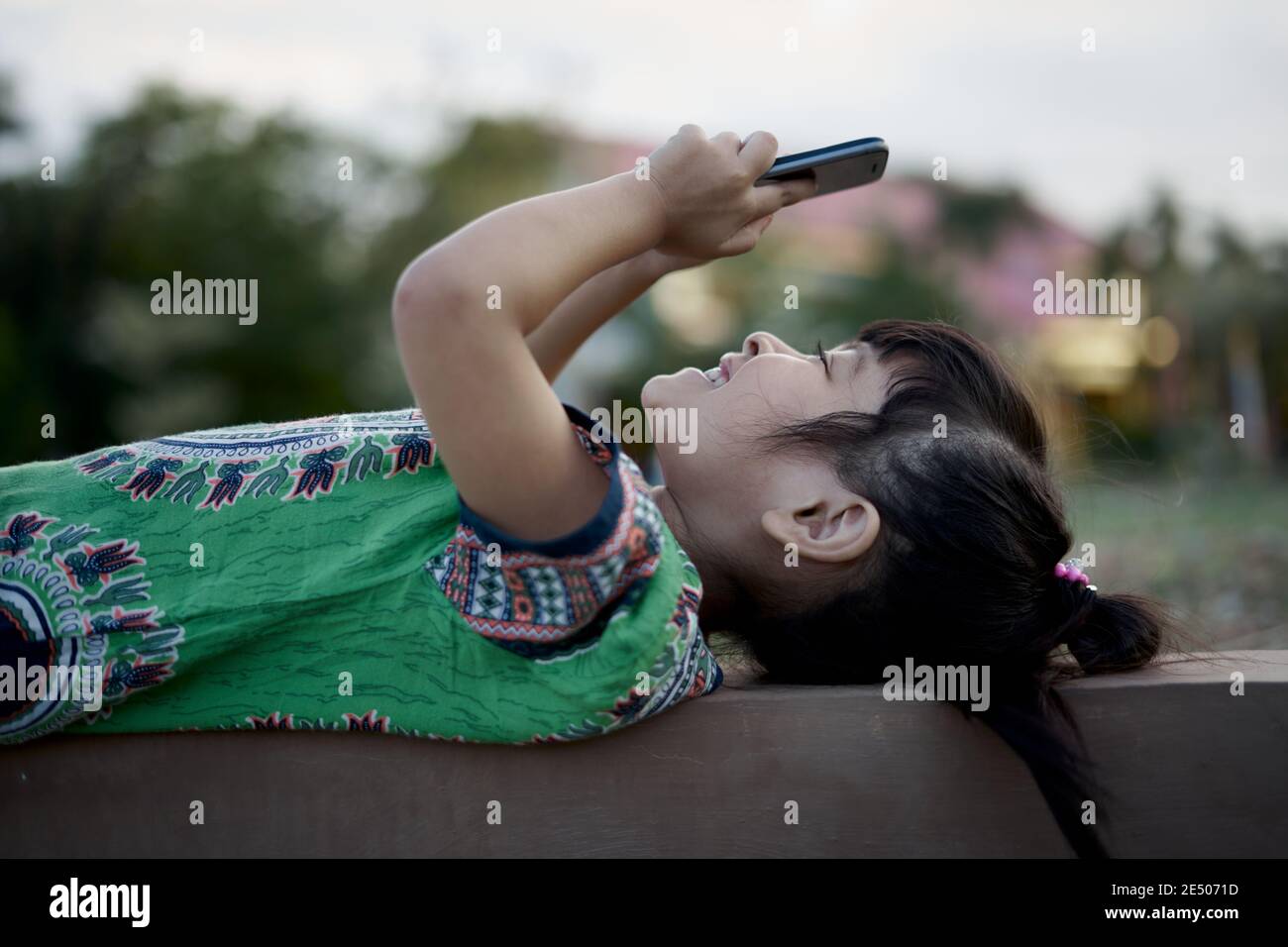Cute little girl lying down and playing with mobile phone at public ...