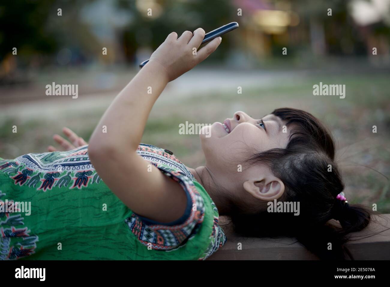 Cute little girl lying down and playing with mobile phone at public ...