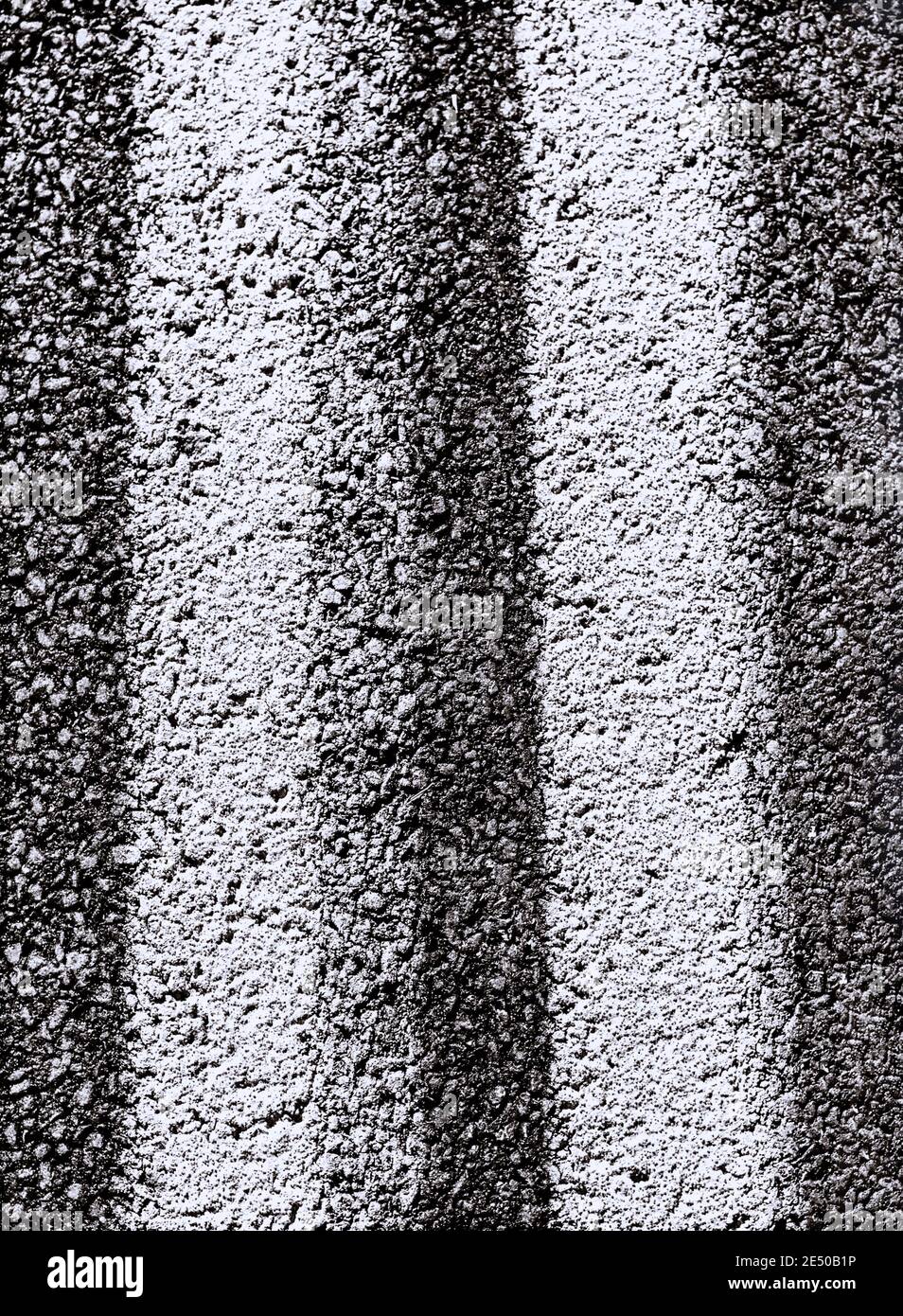 A close up of the double lines of a road reveals its granular texture ...