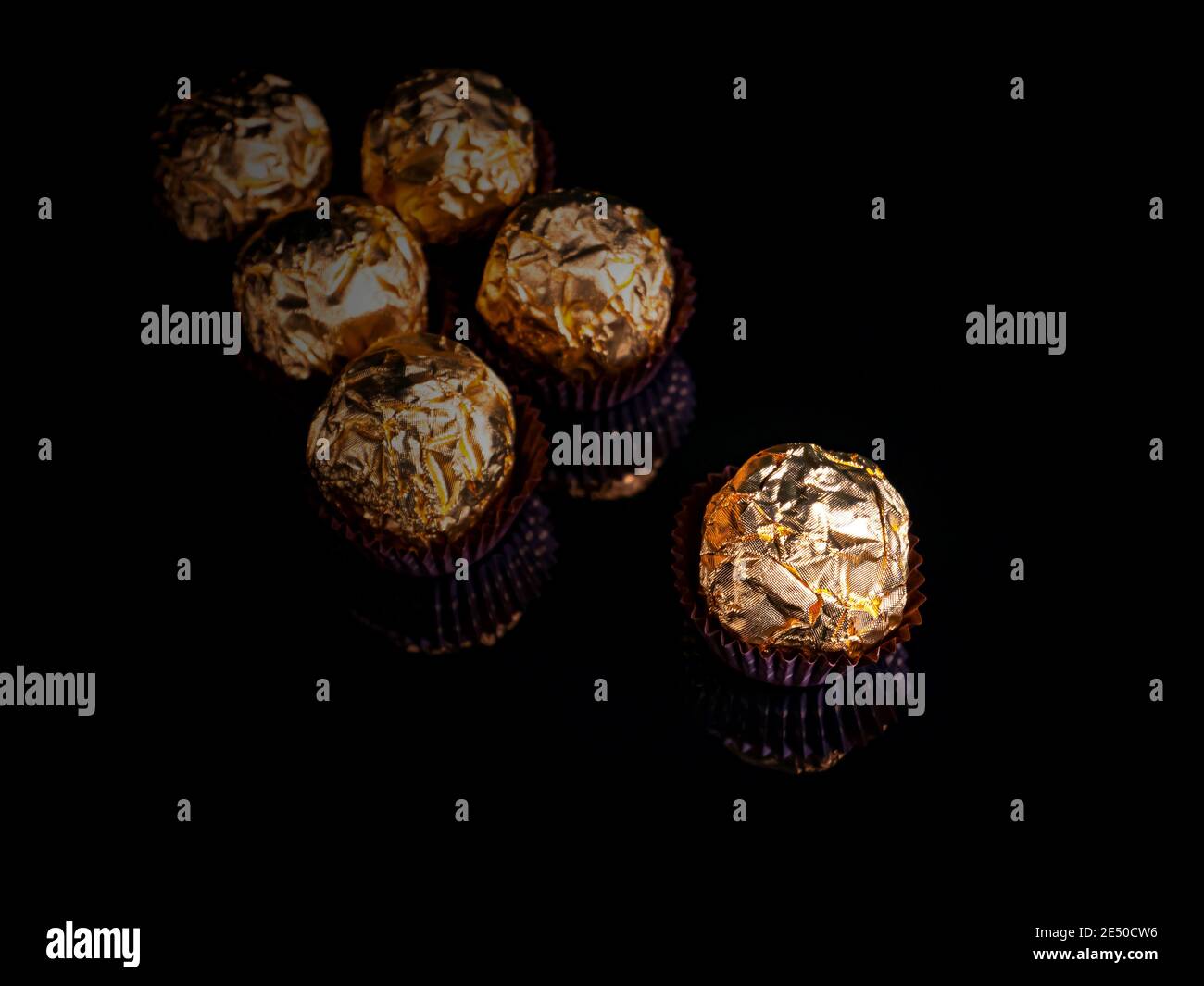 Round candies in golden foil on a black background. Wrapped chocolates ...